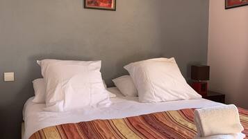 Quarto de hotel com uma cama, duas luminárias fixadas na parede e duas obras de arte emolduradas.