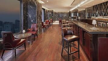 Bar de hotel moderno com assentos de couro, parede de mármore e vista para a cidade.