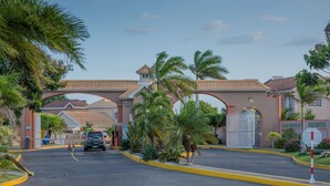 Uma entrada com portão para uma área residencial, com uma estrada bem definida que leva a um edifício com uma placa indicando "Caribbean Estates".