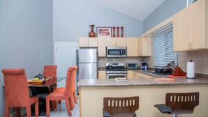 Cozinha compacta equipada com geladeira, micro-ondas, fogão e um pequeno espaço de refeições com duas cadeiras e uma mesa.