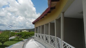 Uma varanda curva com grade, com vista para uma área verde com árvores e céu claro.