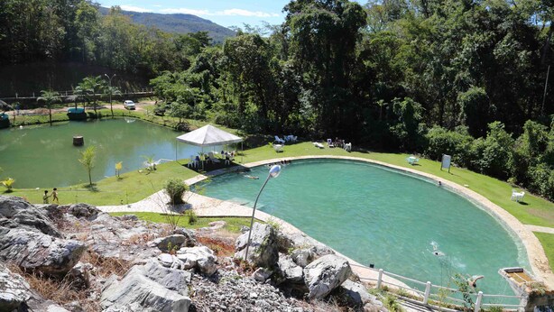 Piscina cercada por vegetação exuberante, com um pequeno pavilhão e espreguiçadeiras.
