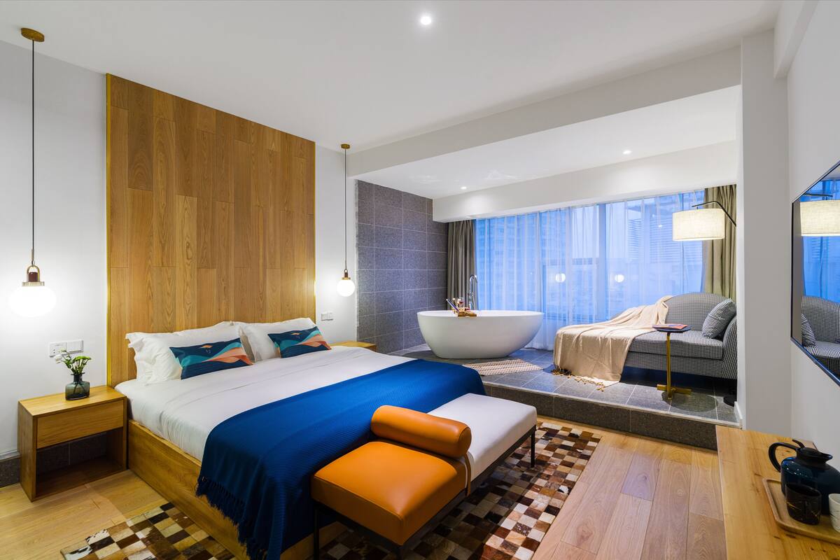 Quarto de hotel moderno com uma cama grande, banheira, sofá e vista para a cidade.