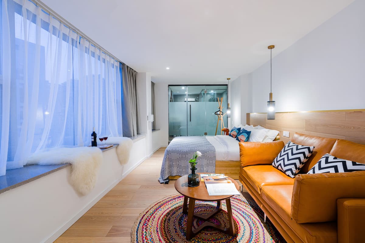 Quarto de hotel moderno com uma janela grande, um sofá, uma cama e uma pequena mesa.