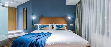 Quarto moderno com cama de madeira, paredes azuis e uma janela grande com cortinas leves.