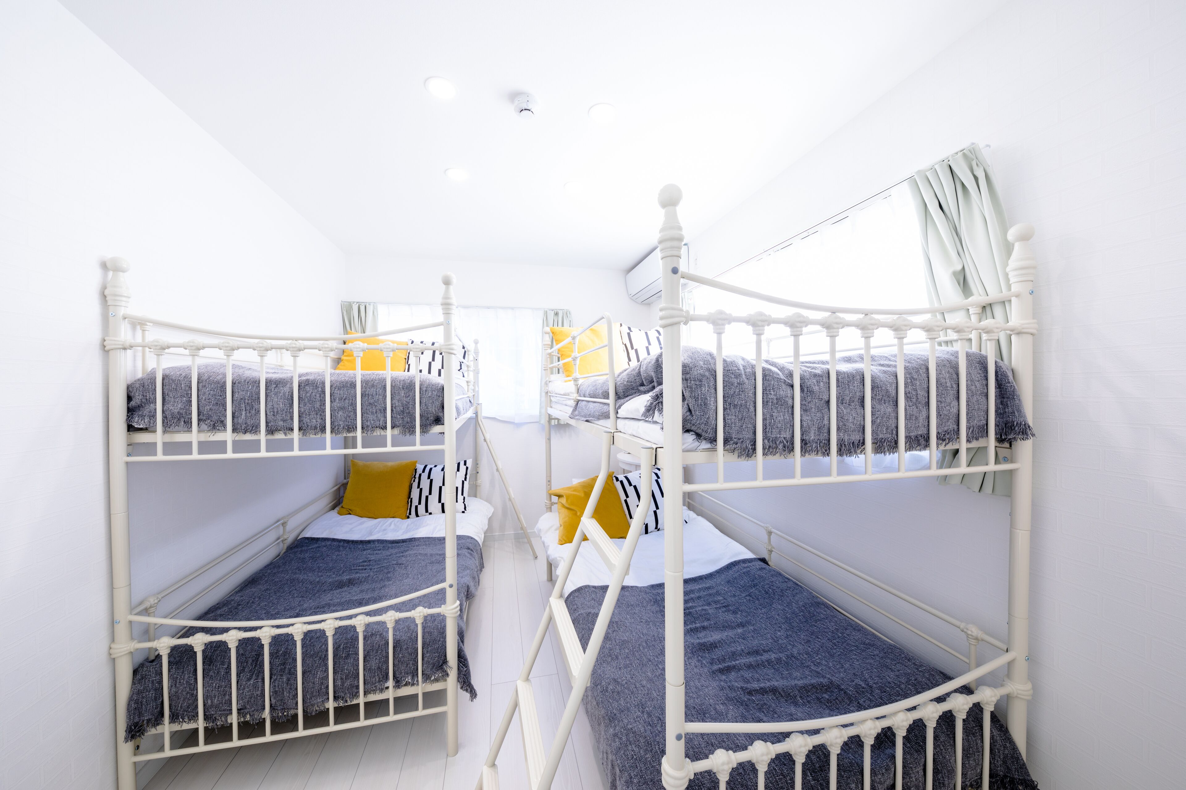 Quarto com beliches dispostos no canto, paredes brancas e teto com iluminação embutida.