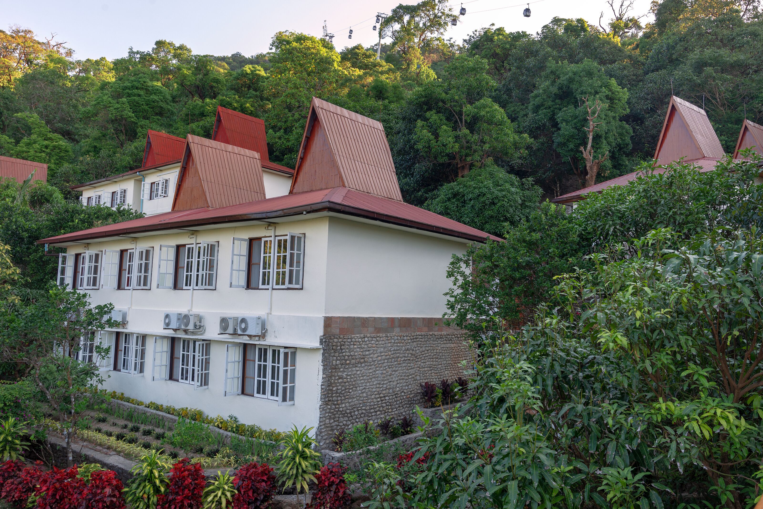Um edifício de vários andares com telhado inclinado, cercado por vegetação exuberante e árvores.