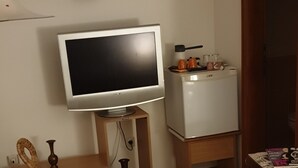 Uma sala de estar com televisão de tela plana, um pequeno frigorífico, uma mesa de jantar com cadeiras e um armário de madeira.