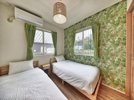Quarto com duas camas, janela com cortinas verdes, ar condicionado na parede e chão de madeira.