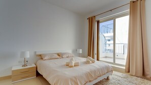 Quarto espaçoso com uma cama grande, mesa de cabeceira, luminária e vista para a varanda.