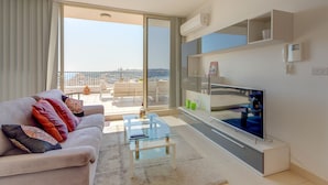 Uma sala de estar moderna com um sofá, uma mesa de centro de vidro e uma televisão de tela plana.