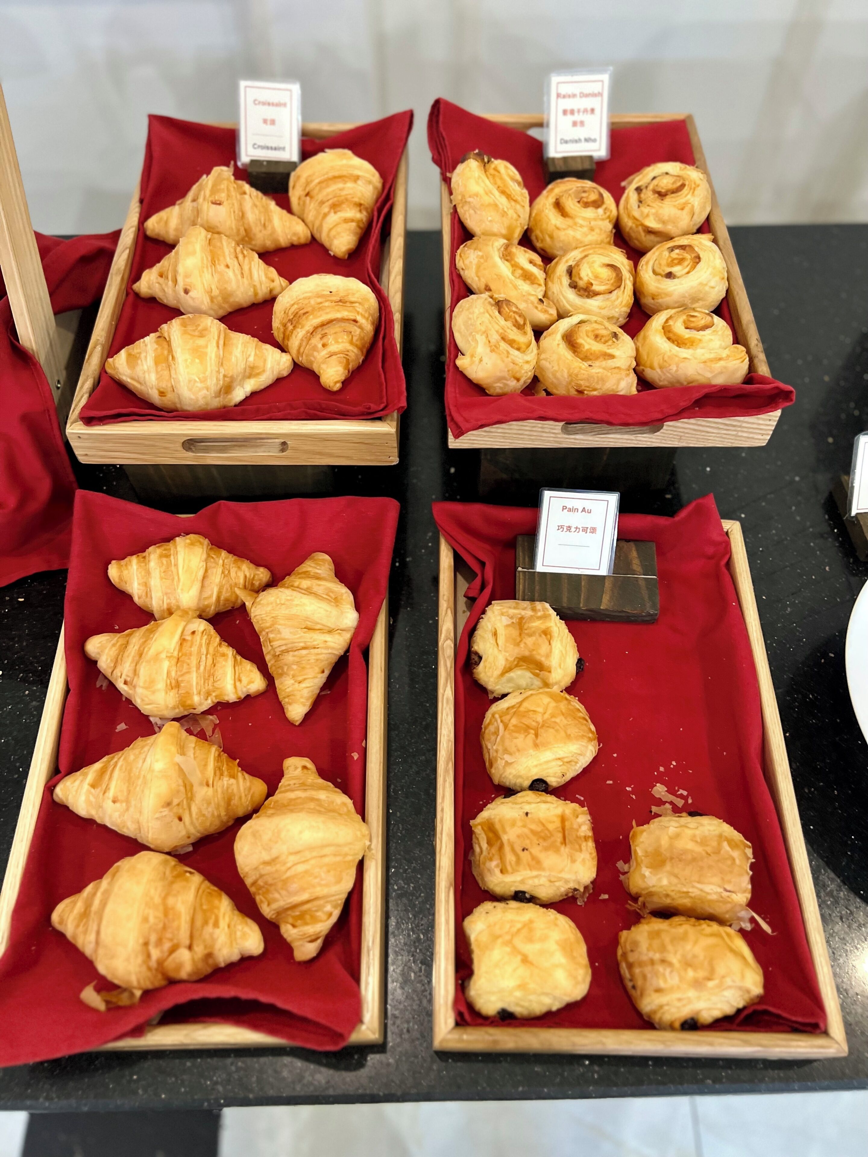 Quatro expositores de madeira com doces sobrepanos vermelhos, cada um identificado com um tipo diferente de pastelaria.
