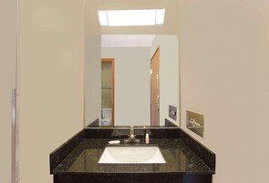 Casa de banho com lavatório de mármore preto, espelho, candeeiro sobre o espelho e porta que dá para outro quarto.