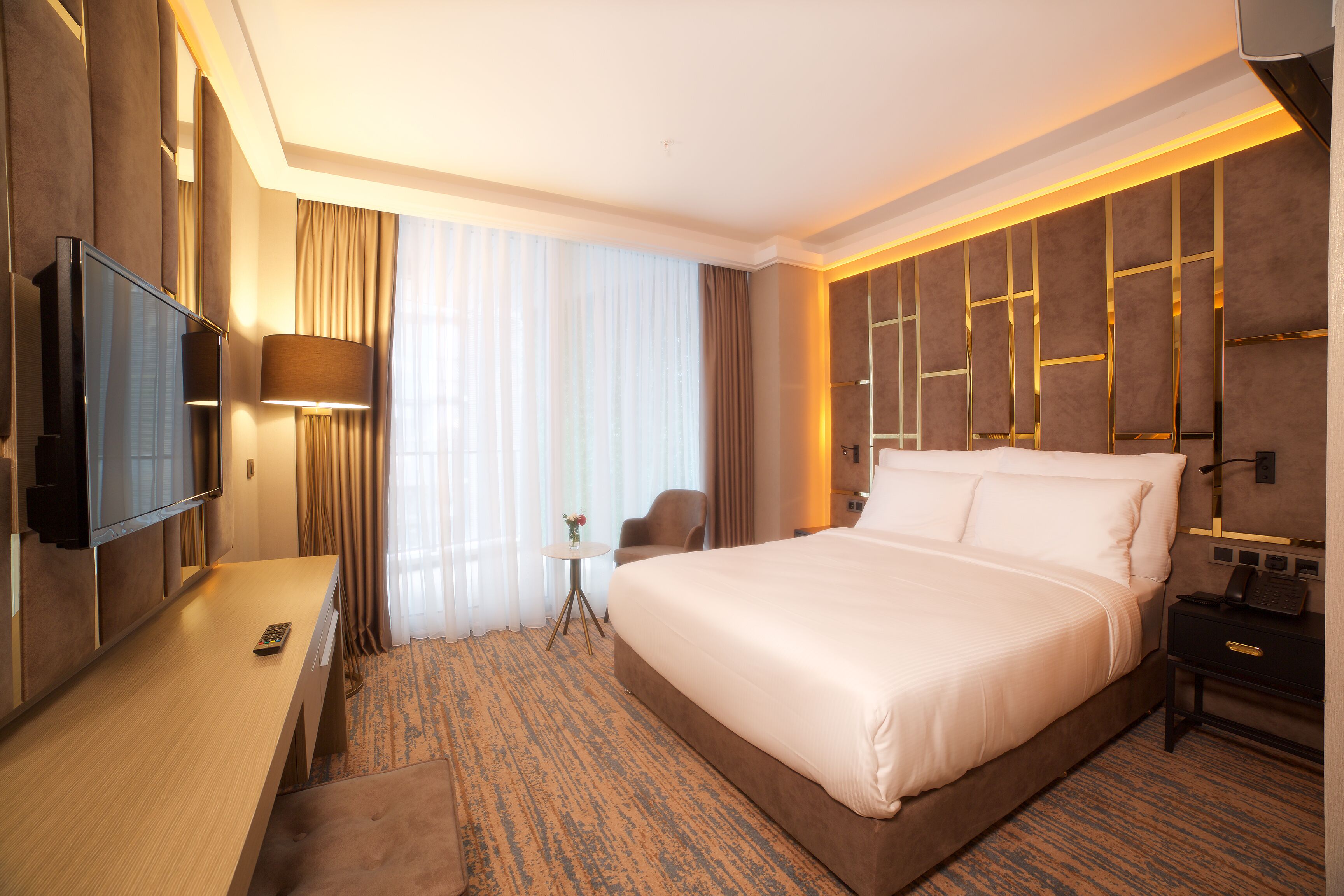 Quarto de hotel com uma cama grande, uma televisão, uma escrivaninha e uma pequena mesa com abajur.