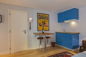 Uma cozinha compacta com um banquinho de madeira, um armário azul e um cartaz vintage na parede.