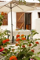 Um pátio externo com mesa, cadeiras e guarda-sol.