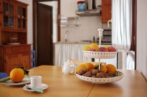 Uma mesa de jantar com uma chaleira branca, uma xícara, uma tigela de frutas e um prato com uma laranja.