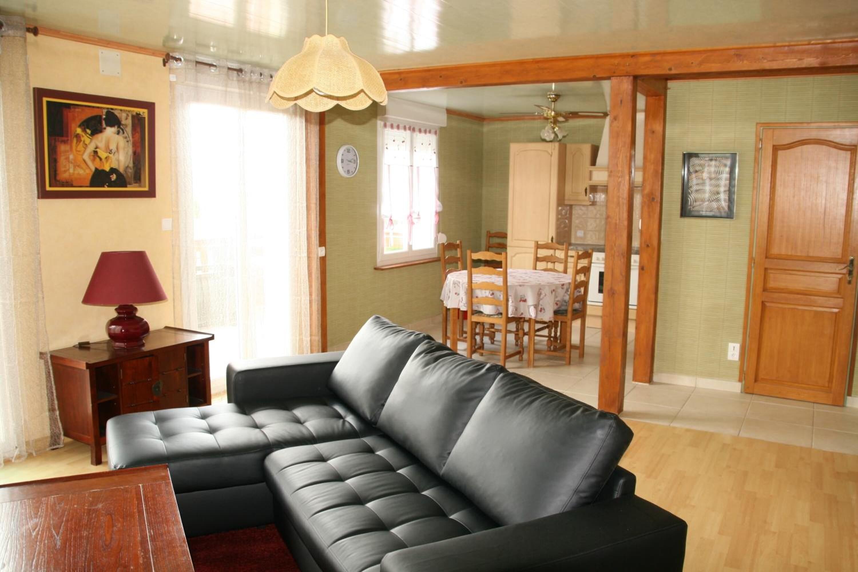 Uma sala de estar com sofá, um armário de madeira, uma luminária e uma área de refeições ao fundo.