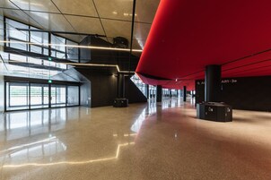 Interior espaçoso e moderno, com piso lustroso, janelas amplas e um detalhe arquitetônico vermelho marcante.