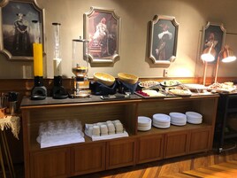 Uma mesa de buffet com diversos alimentos, utensílios de servir e dispensadores de bebidas.