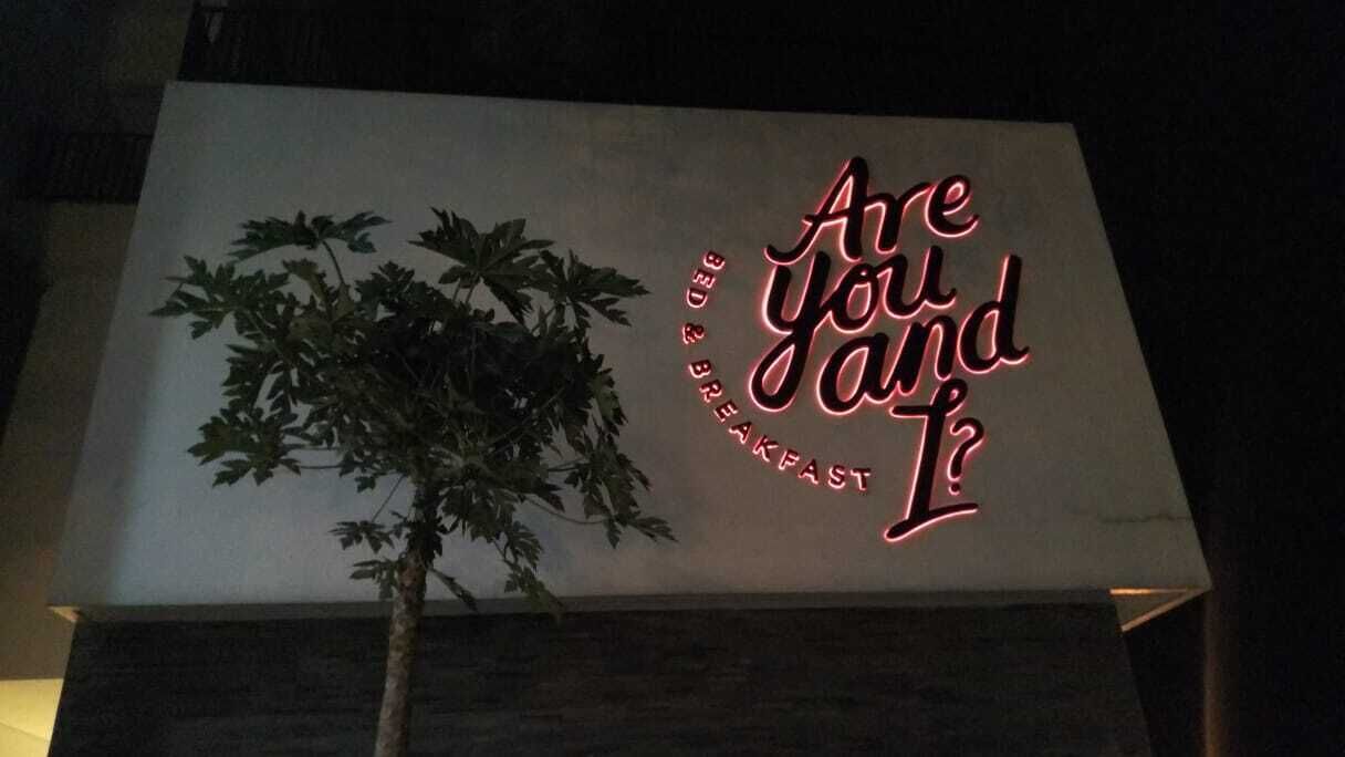 Um letreiro de neon com os dizeres 'Are you and I?' e 'Bom Café da Manhã' em uma fachada de prédio.