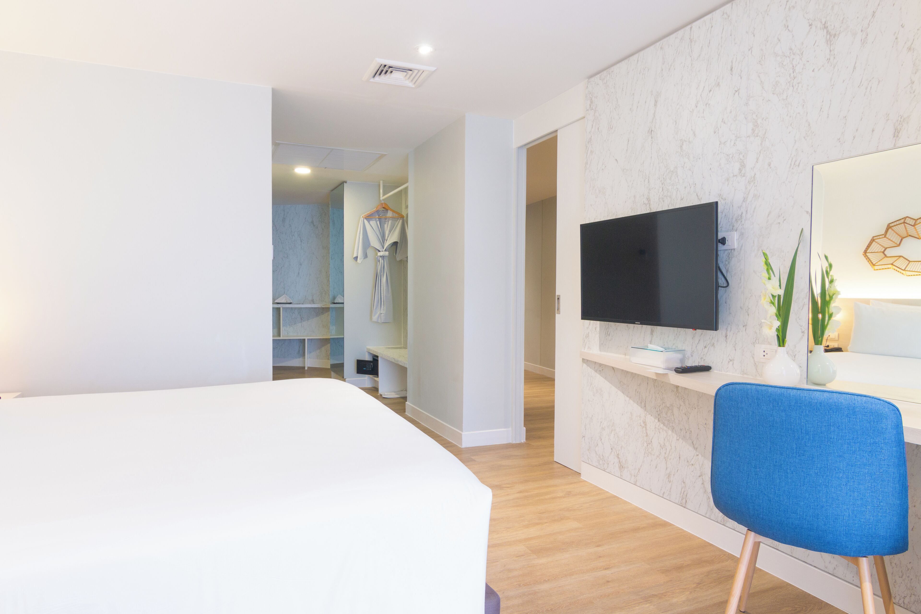 Quarto de hotel moderno com uma cama grande, uma escrivaninha com cadeira, uma TV de tela plana e uma parede de mármore.