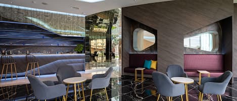 Um lobby moderno com piso de mármore, áreas de estar com sofás e cadeiras, um espaço de bar e um espelho grande.