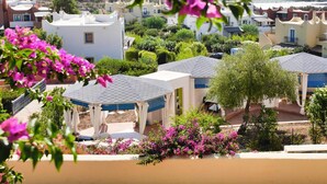 Zona residencial com edifícios brancos, um coreto e flores cor-de-rosa.