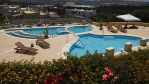 Uma área de piscina com várias piscinas, espreguiçadeiras e um jardim de flores.