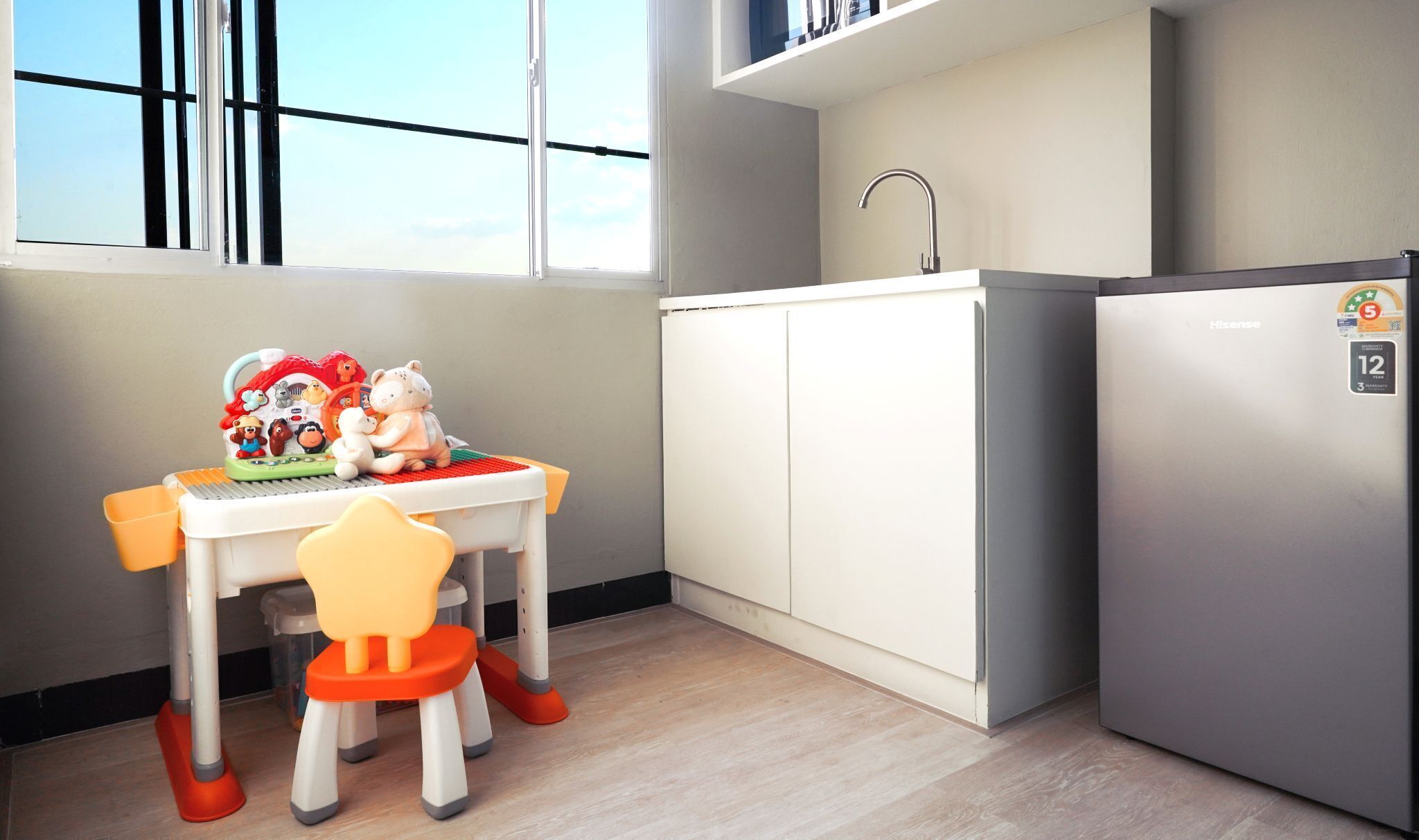 Cozinha moderna com geladeira de aço inoxidável, armário branco e janela com vista para o céu.