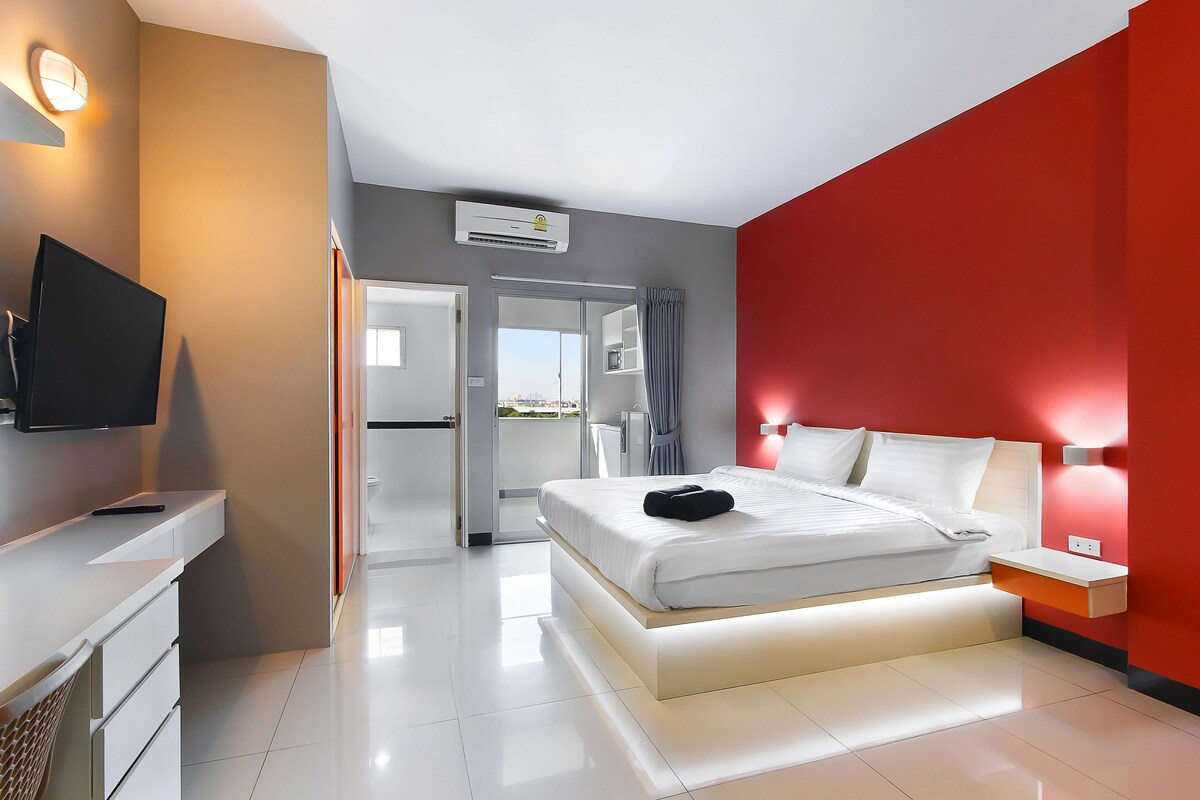 Quarto moderno com cama, mesas de cabeceira, televisão e vista para o exterior.