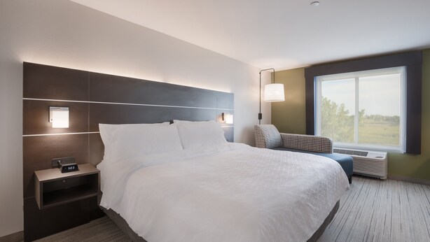 Quarto de hotel moderno com cama grande, mesinhas de cabeceira, luminária e uma janela ampla com vista.