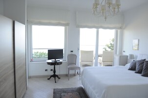 Quarto de hotel com uma cama grande, televisão, cadeira e varanda com vista.