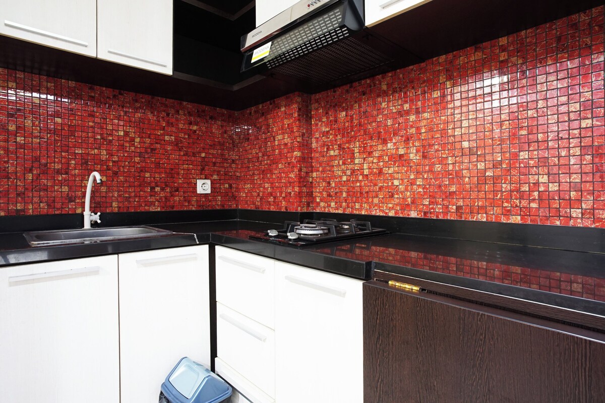 Cozinha com painel de azulejos vermelhos, armários brancos e bancada preta.