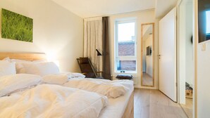 Quarto de hotel com cama grande, uma cadeira, janela com cortinas e porta.