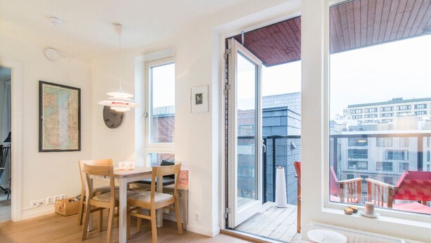 Um apartamento moderno com área de jantar, varanda com cadeiras vermelhas e vista para edifícios.