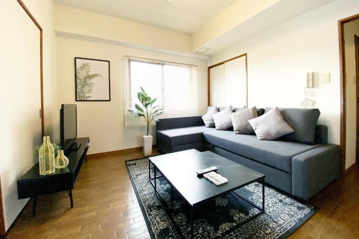 Uma sala de estar moderna com um sofá modular cinza, uma mesa de centro preta e uma televisão de tela plana em um suporte preto.