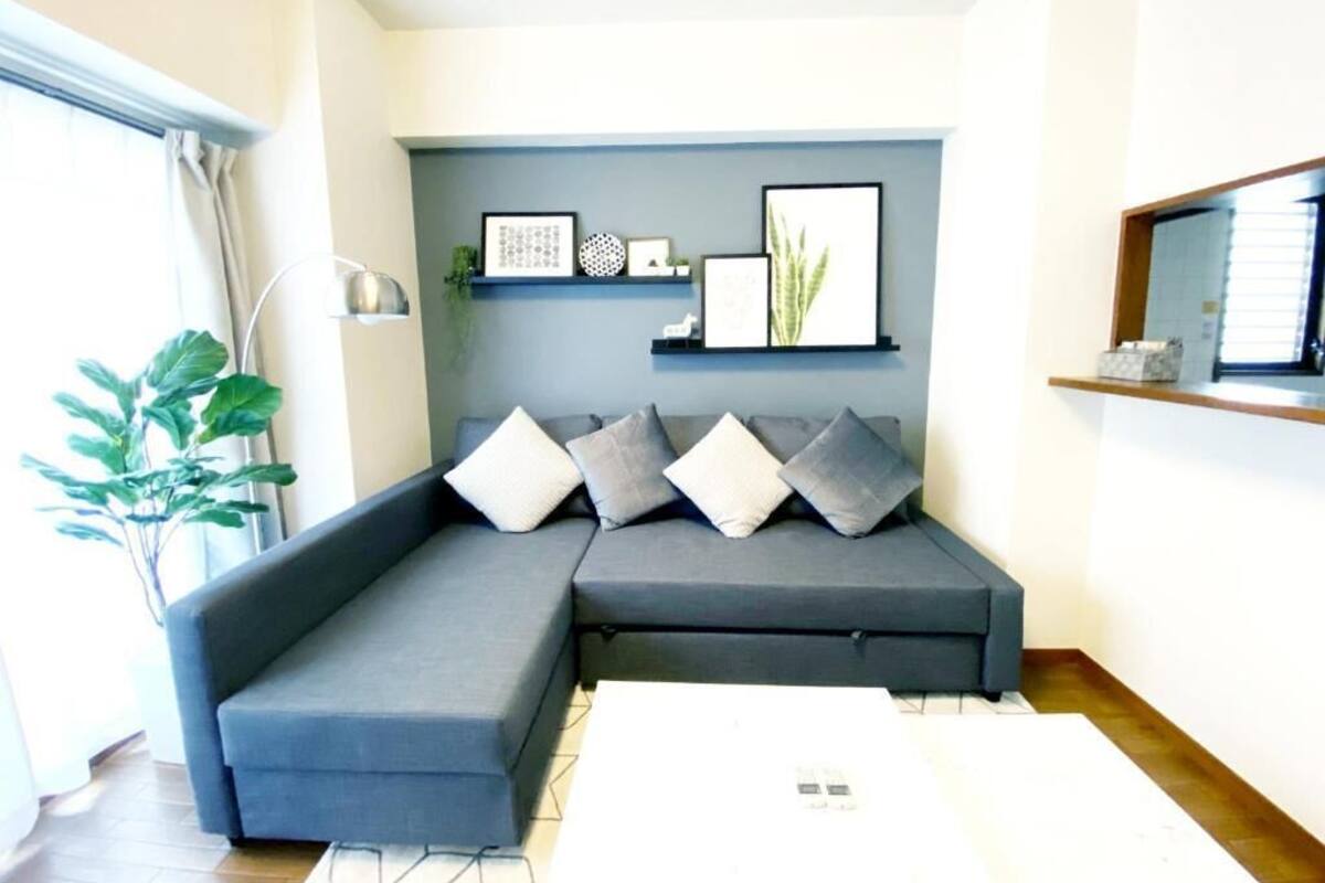 Uma sala de estar moderna com um sofá seccional cinza, uma mesa de centro branca e uma estante fixada na parede com fotografias emolduradas.