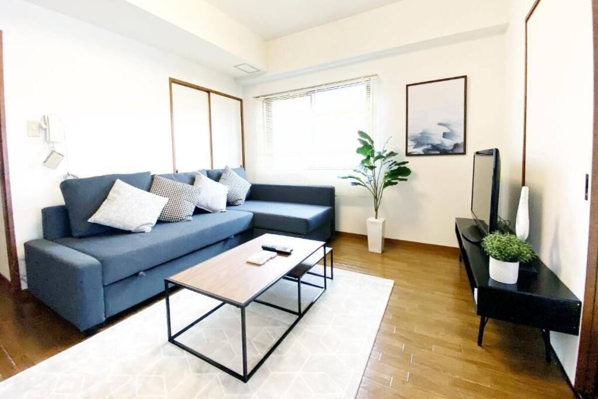 Uma sala de estar moderna com um sofá seccional, uma mesa de centro, uma televisão em um móvel e um vaso com planta.