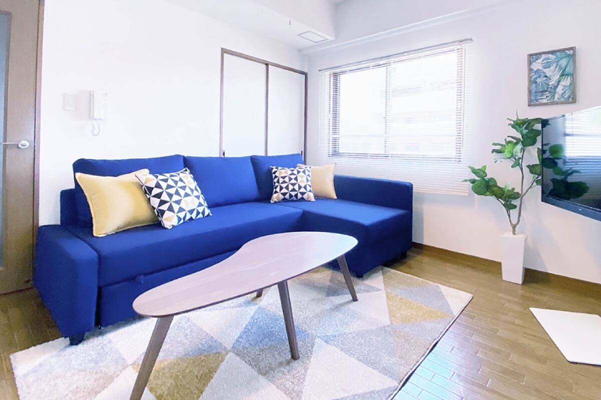 Uma sala de estar com um sofá azul, uma mesa de centro, uma televisão e uma planta.