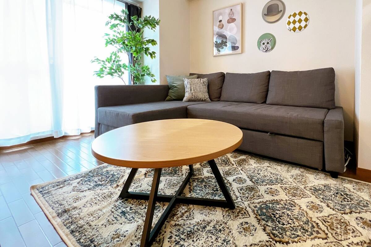 Uma sala de estar com sofá, mesa de centro redonda, tapete estampado e obras de arte nas paredes.