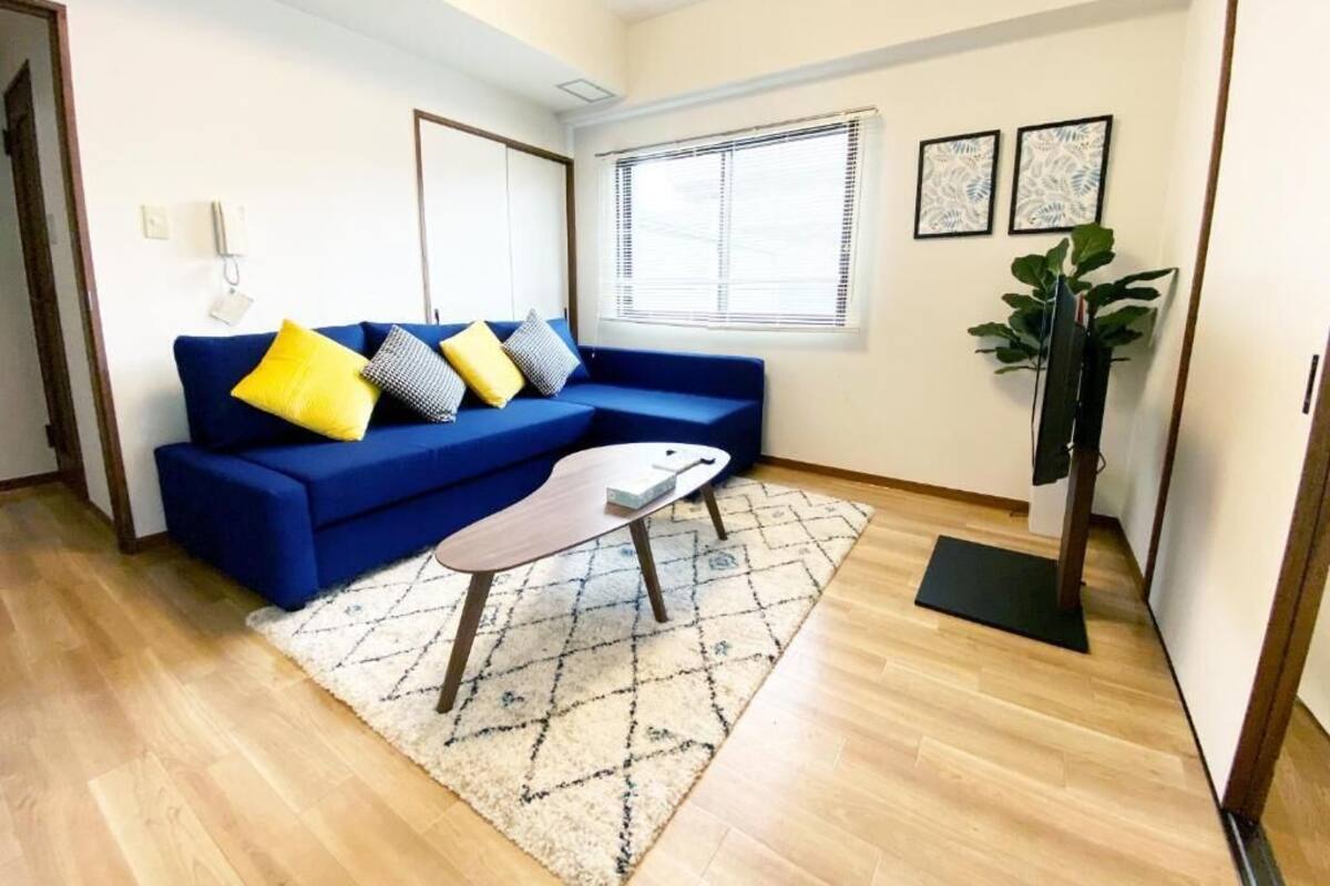Uma sala de estar com um sofá azul, uma mesa de centro, um tapete estampado e uma janela com persianas.
