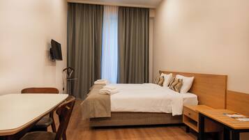 Quarto de hotel com uma cama, uma mesa, uma cadeira e uma televisão na parede.