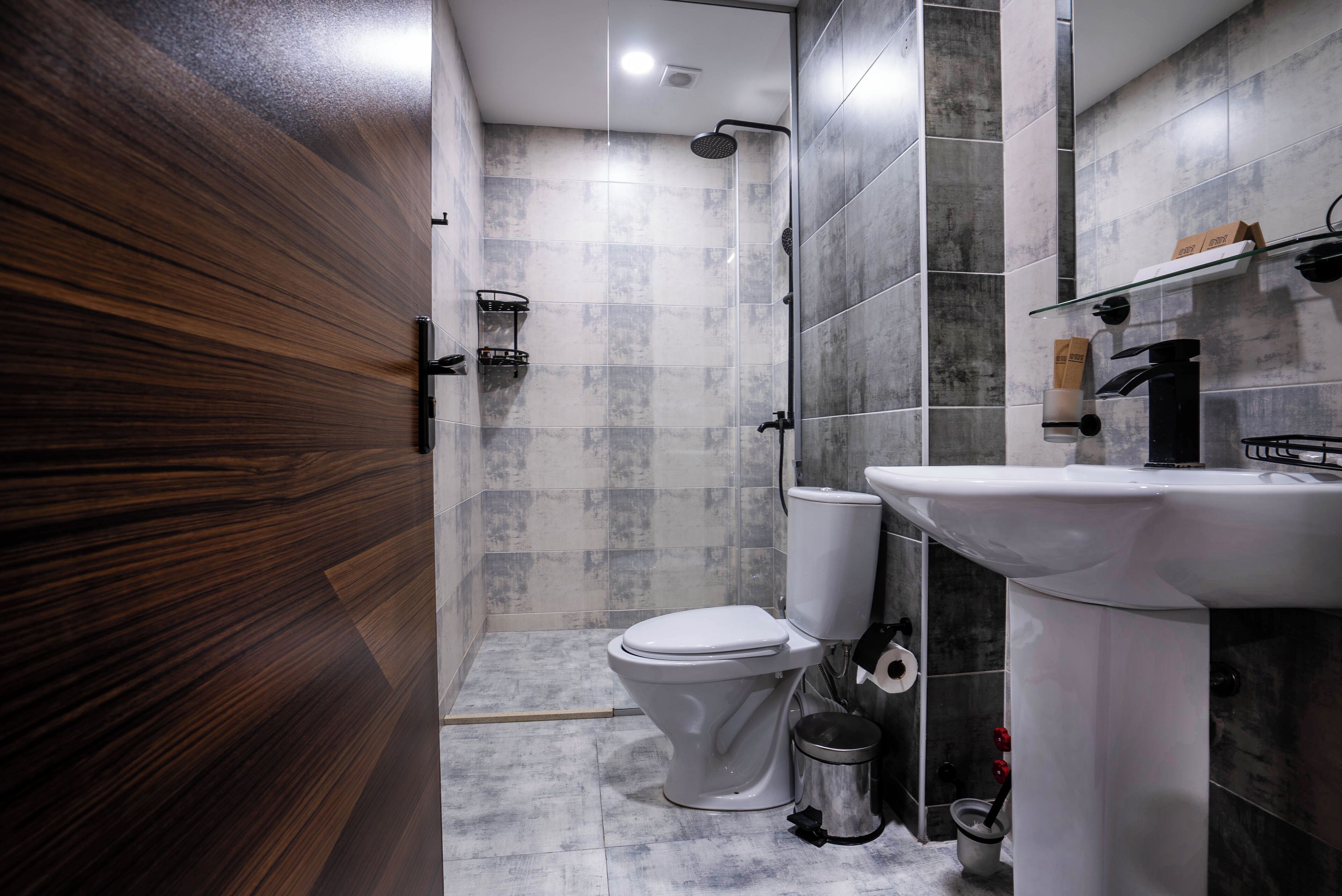 Uma casa de banho moderna com porta de madeira, chuveiro, sanita e lavatório.