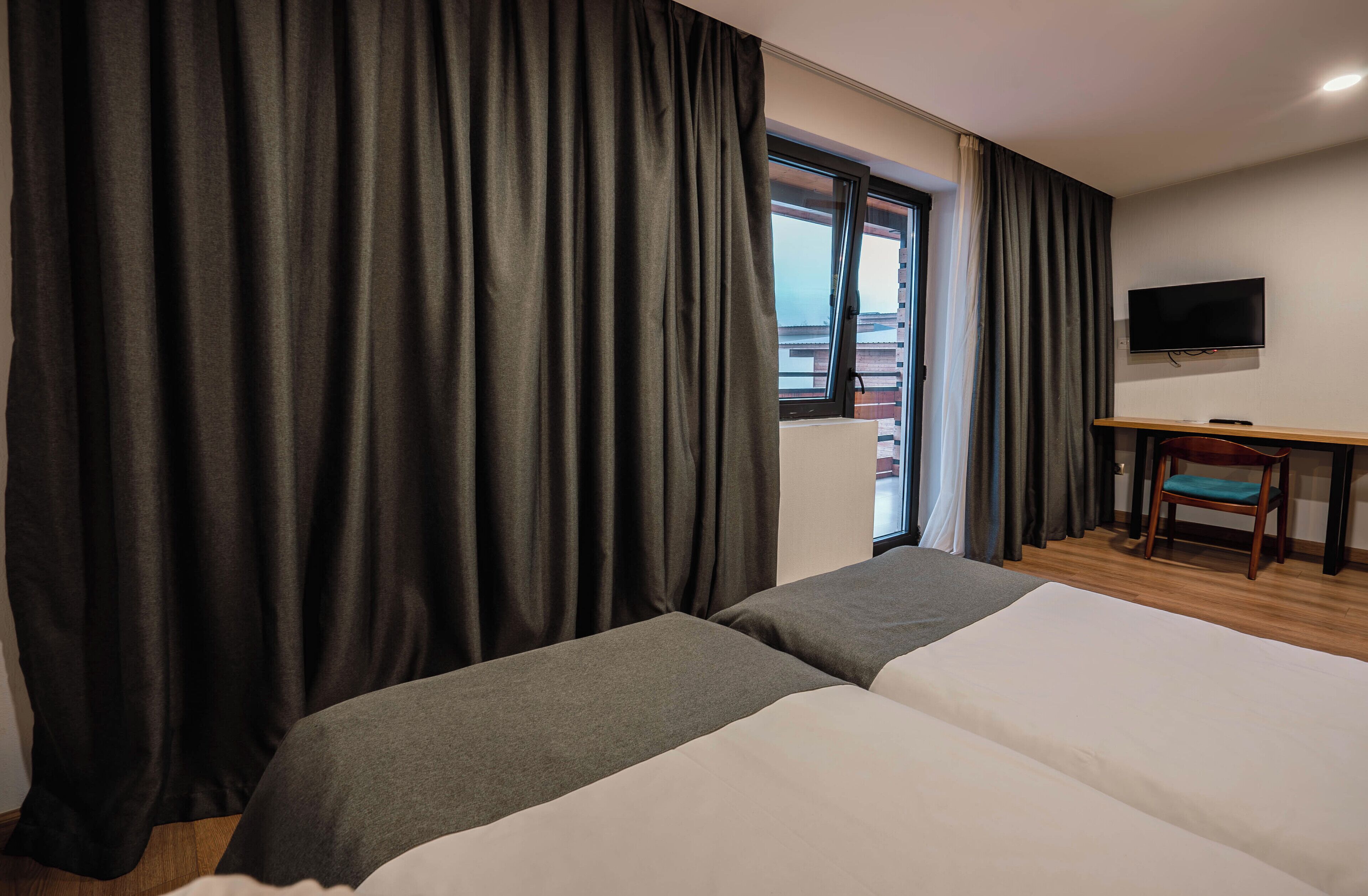 Quarto de hotel com duas camas, uma televisão na parede e uma escrivaninha com uma cadeira.