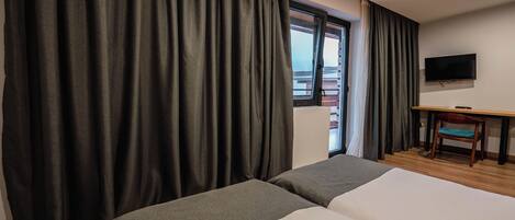 Quarto de hotel com duas camas, uma televisão na parede e uma escrivaninha com uma cadeira.
