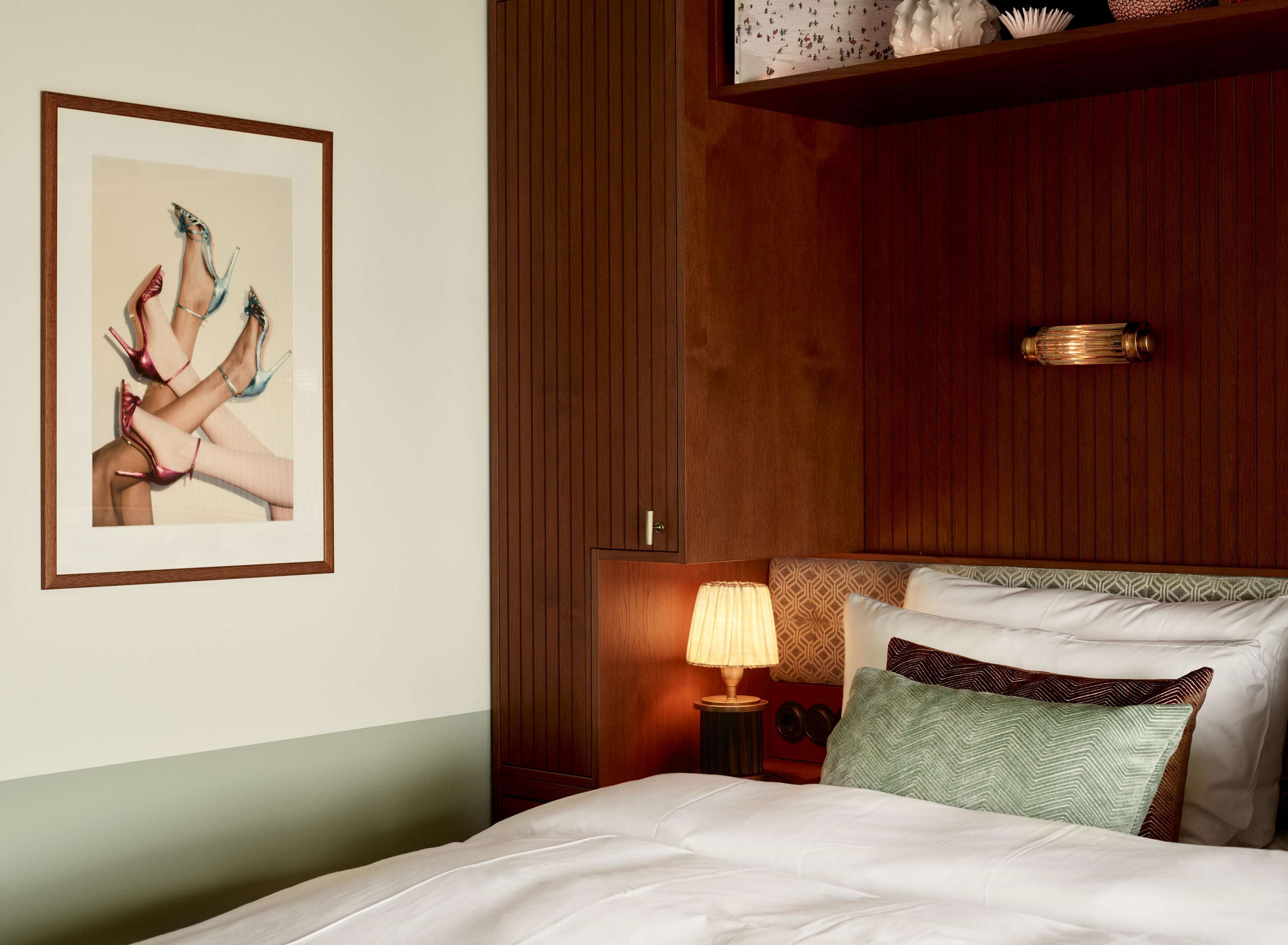 Quarto de hotel com cama, mesa de cabeceira com abajur, quadro na parede e painéis de madeira.