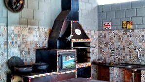 Uma cozinha rústica ao ar livre, com parede de tijolos, chaminé e piso de azulejos.