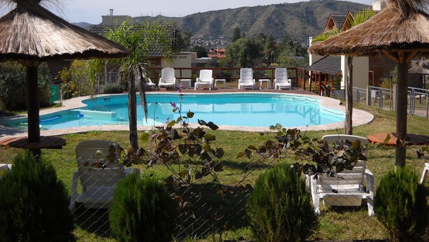 Piscina com espreguiçadeiras e guarda-sóis de palha, cercada por vegetação e colinas ao fundo.