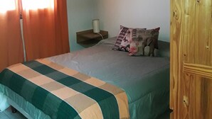 Quarto com cama, guarda-roupa de madeira, mesa de cabeceira e ventoinha no teto.
